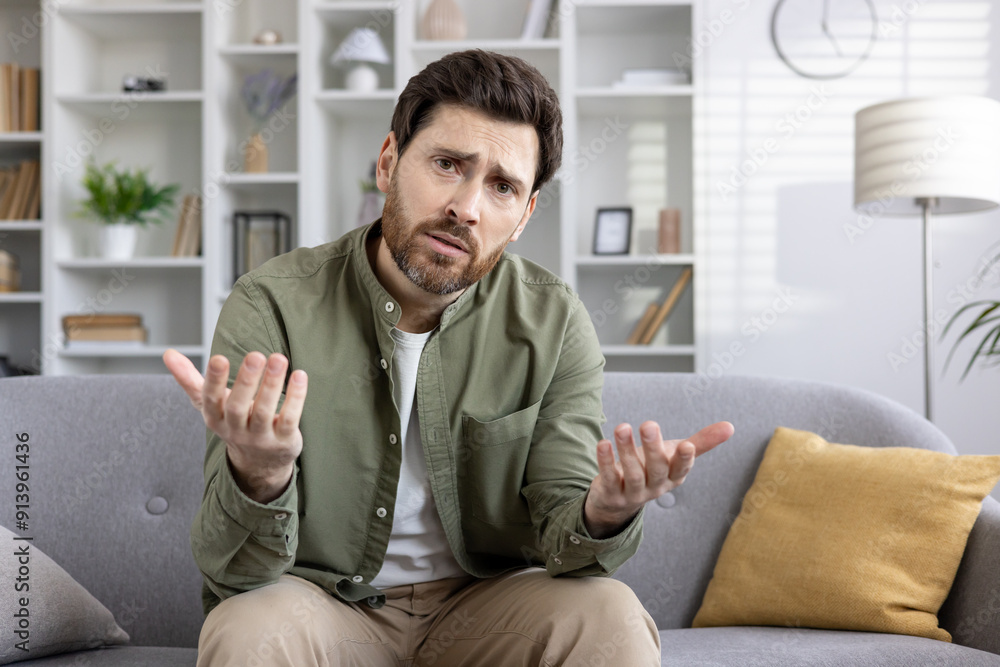 Man sitting on sofa expressing confusion during video call using phone ...