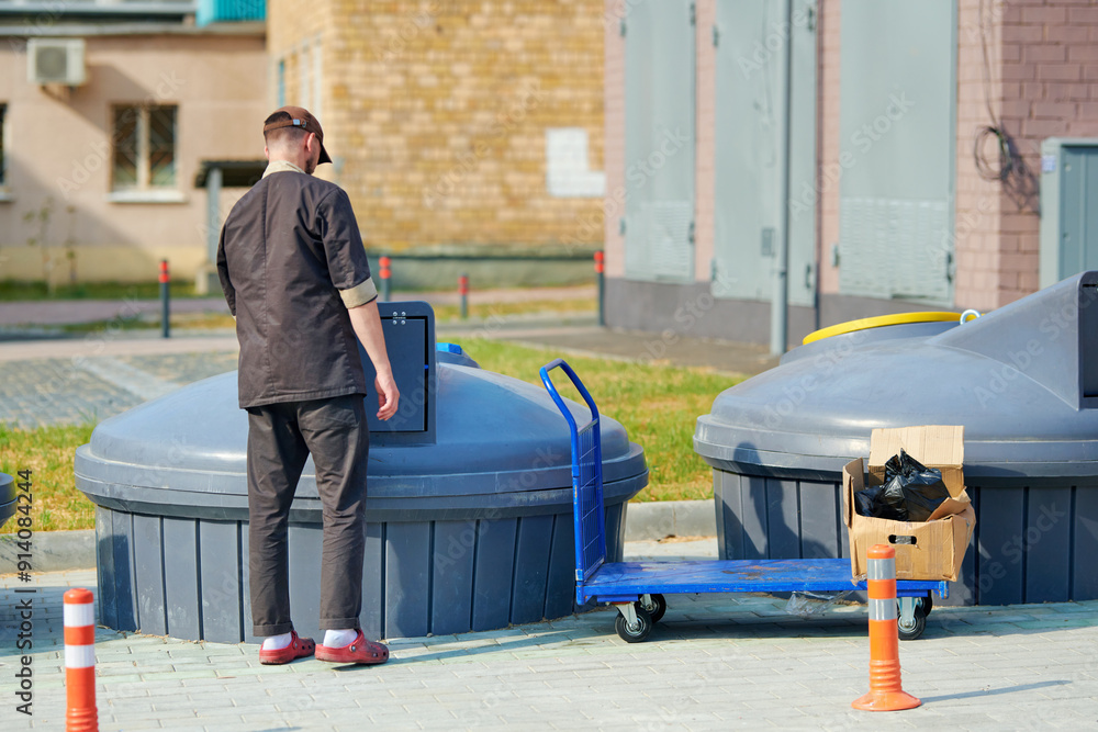 Man in uniform throwing garbage into underground trash containers ...