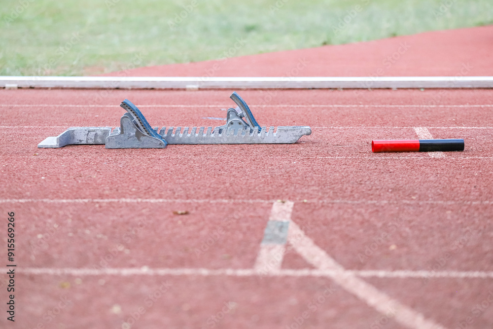Poster Close-up of starting blocks and relay baton on an empty running ...