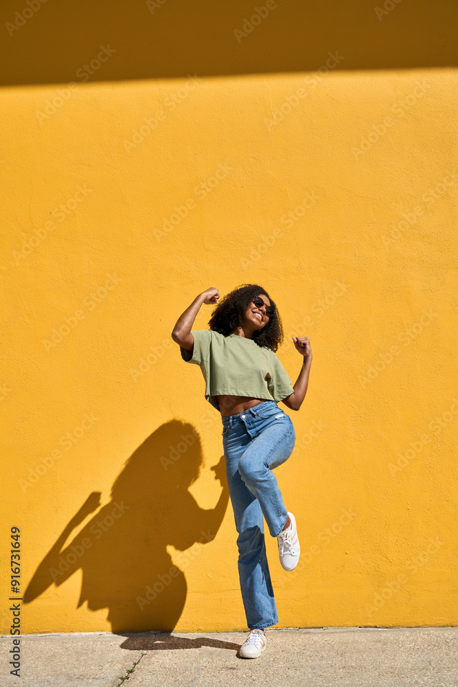 Happy young African American woman winner jumping standing at yellow ...