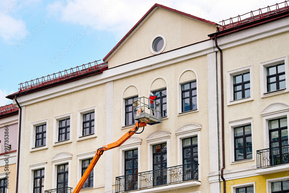 Worker washing windows with crane bucket lift. Laborer on cherry picker washing windows at ...