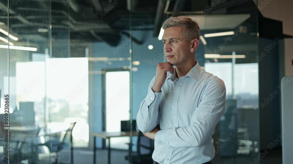 Thoughtful male business person thinking about work standing by window ...