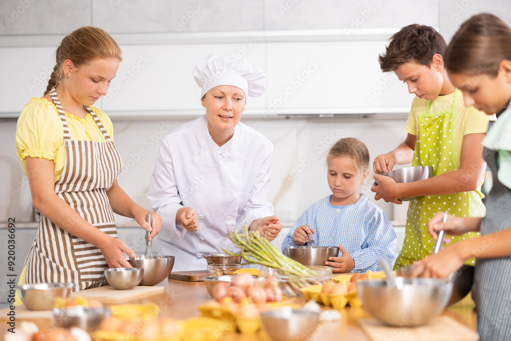Adult woman chef at master class teaches group of children how to cook ...