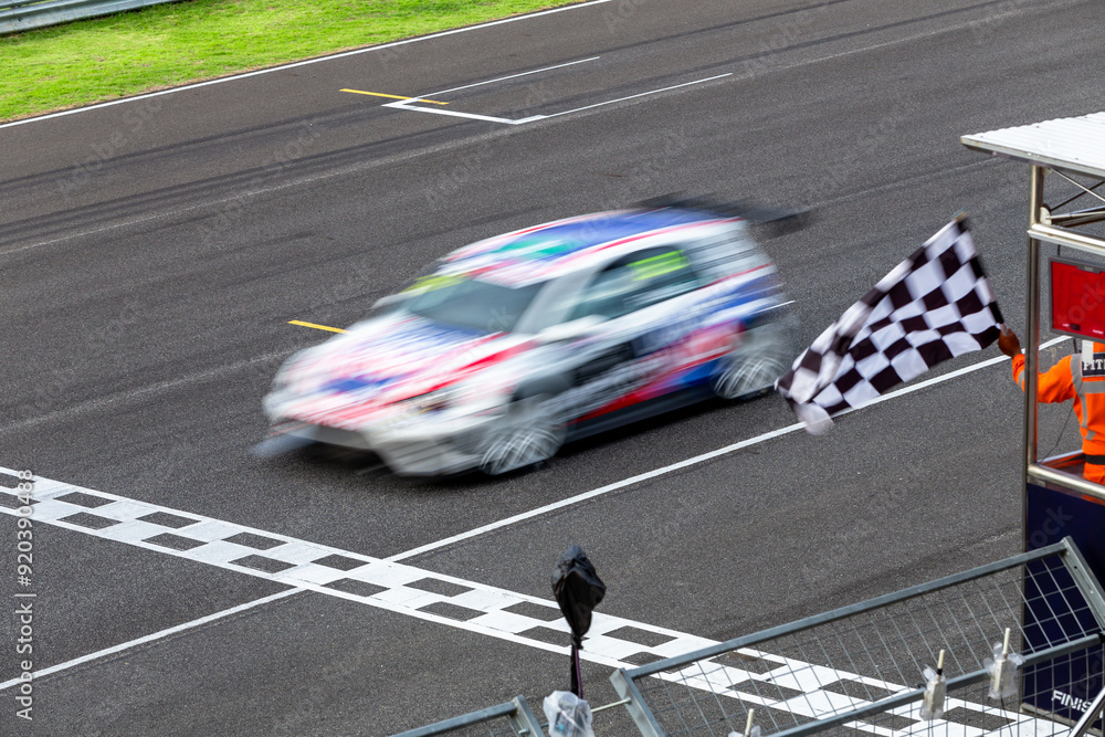 Race car crossing finish line on track and pass checkered race flag ...