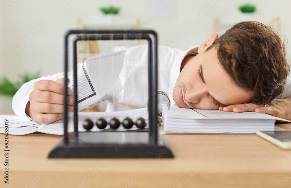 Tired businessman sitting at work desk with Newton's cradle pendulum at ...