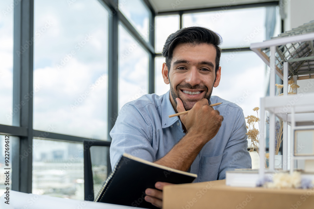 Smiling smart architect engineer looking at camera while sitting near ...