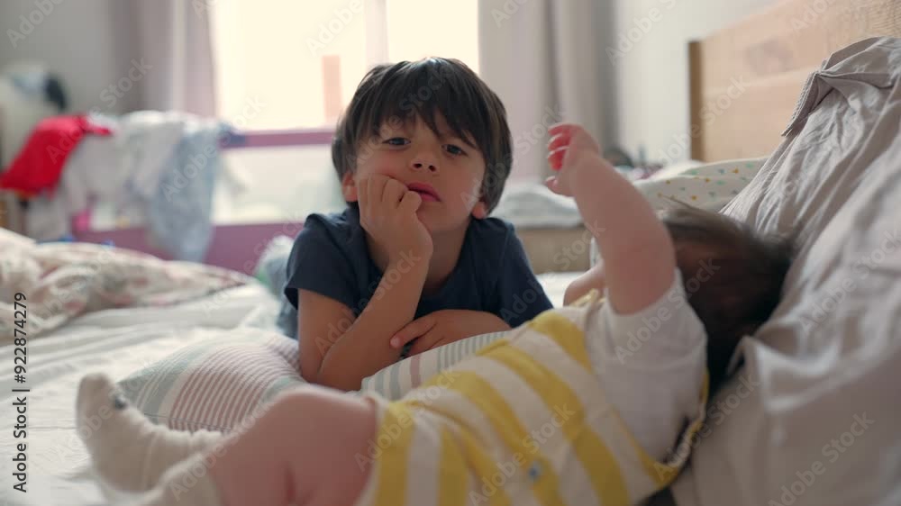 Older sibling lying beside a baby sibling on a bed, engaging in a warm ...