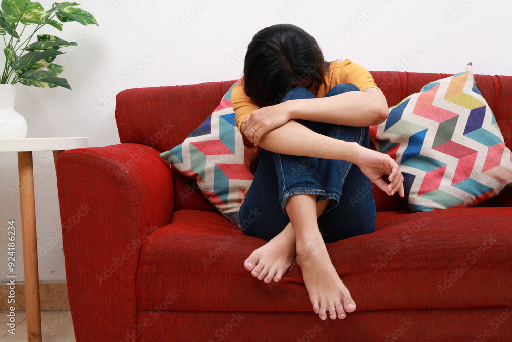 Depressed young Asian woman sitting on a couch with her legs crossed ...