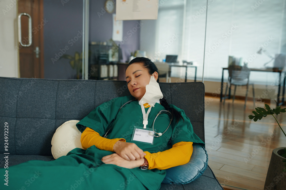 Nurse relaxing on couch, wearing uniform with name tag, taking break in ...