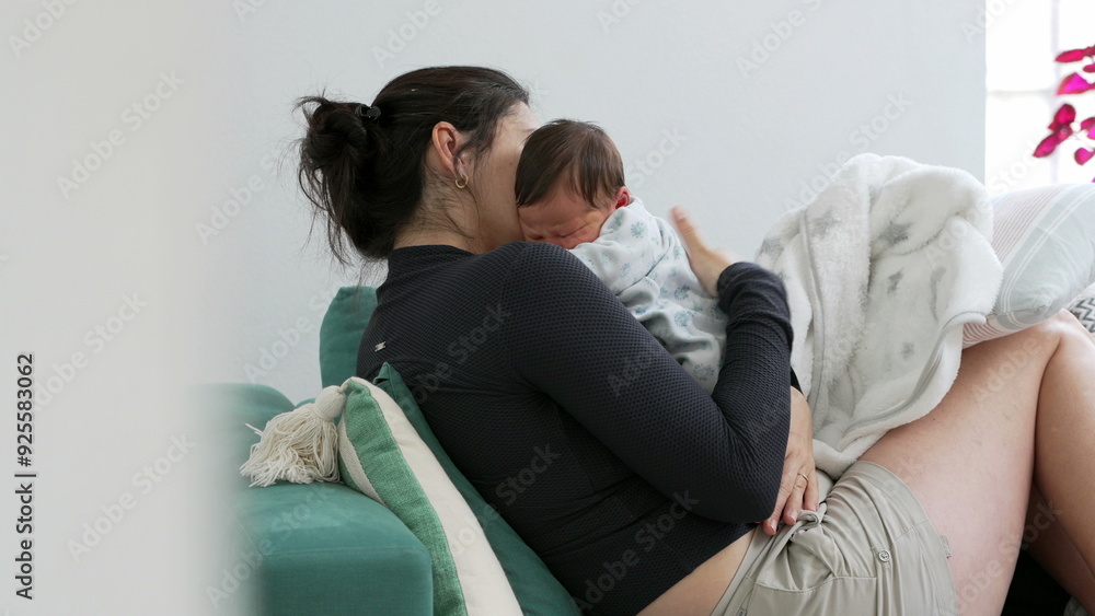 Mother tapping her newborn baby on the back while sitting on the couch ...