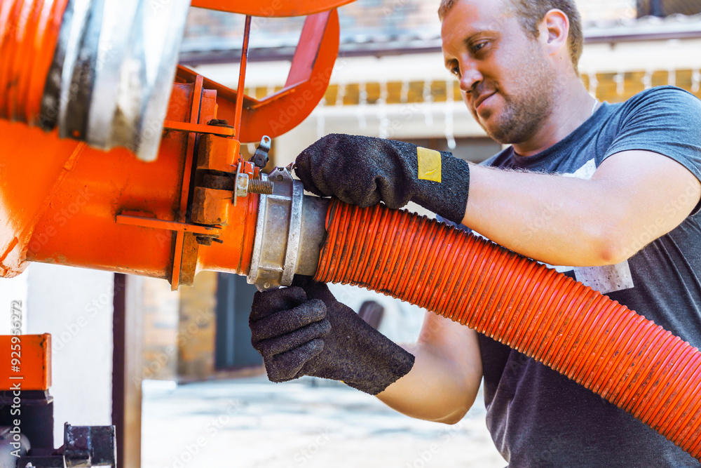 workman connects a suction hose to a sewage tanker truck. Septic tank ...