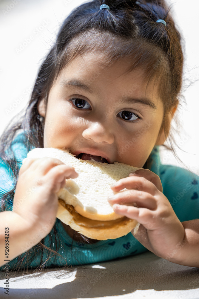 A young girl is eating a sandwich with a jar of peanut butter next to ...