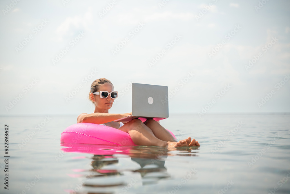 A woman is sitting on a pink inflatable raft in the ocean, using a ...