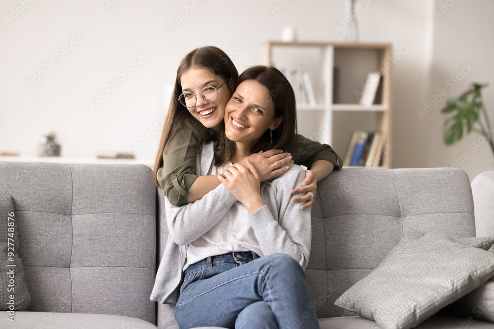 Cheerful middle-aged mother with adolescent daughter enjoy family weekend at home, looking at ...