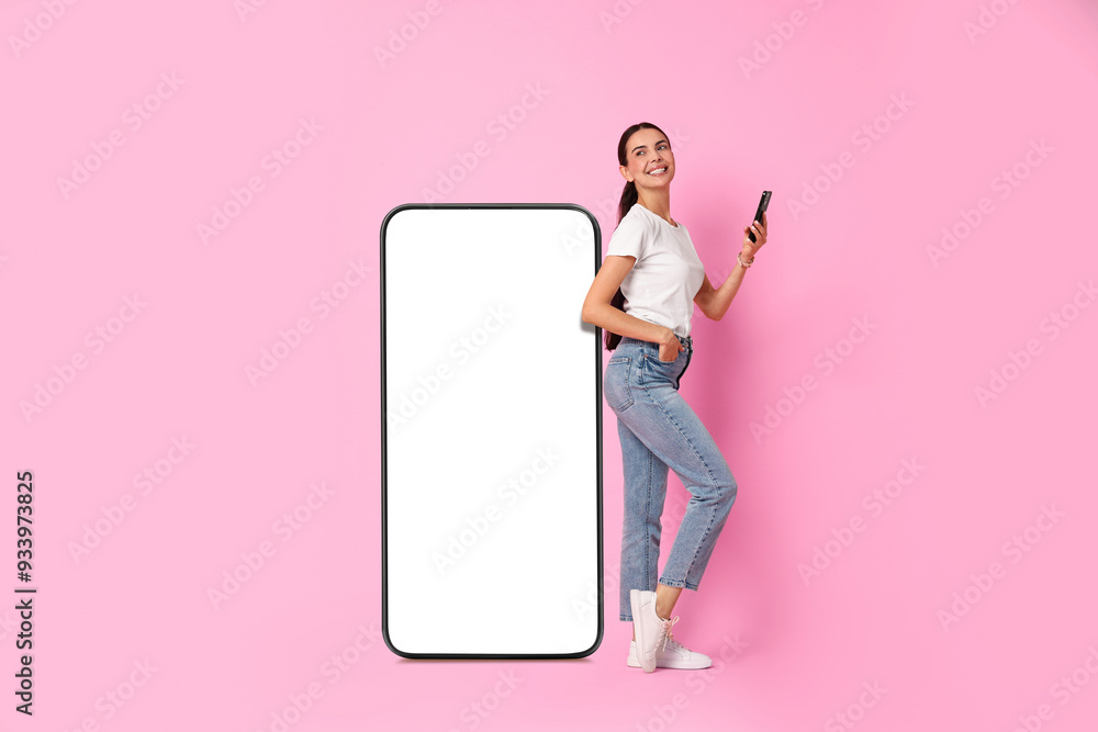 Beautiful young woman with smartphone standing near big mobile phone ...