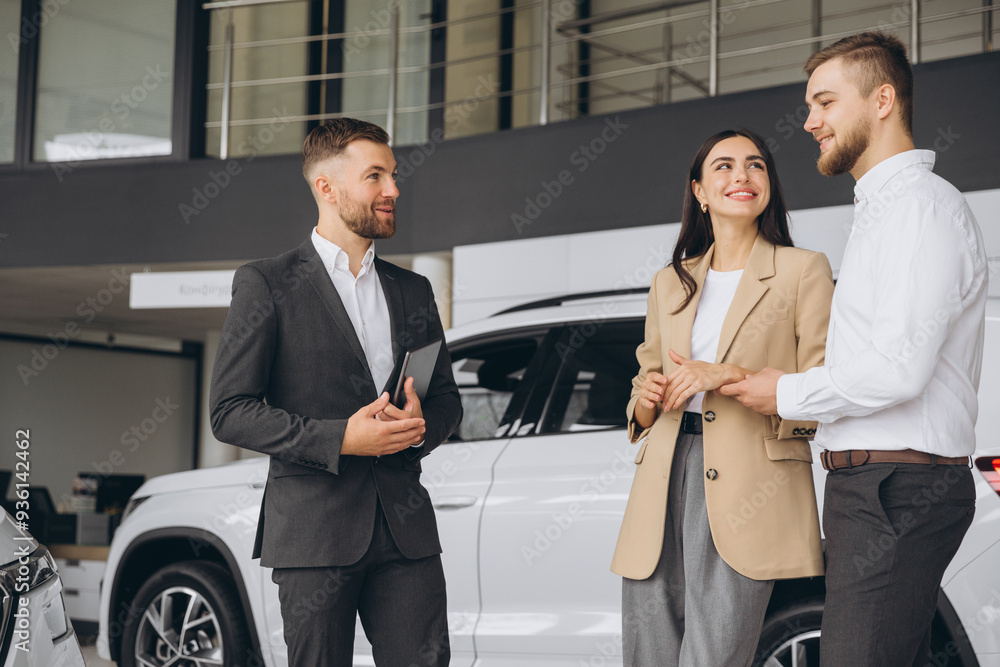 A well-dressed salesman is presenting information to couple in a car ...