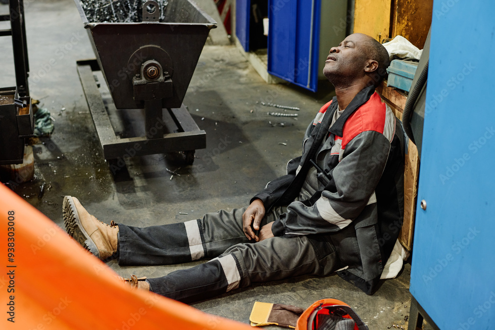 Worker sitting against wall in industrial setting, appearing exhausted ...