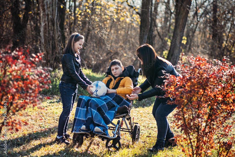 Mother and sibling engaging child in wheelchair in outdoor play with ...