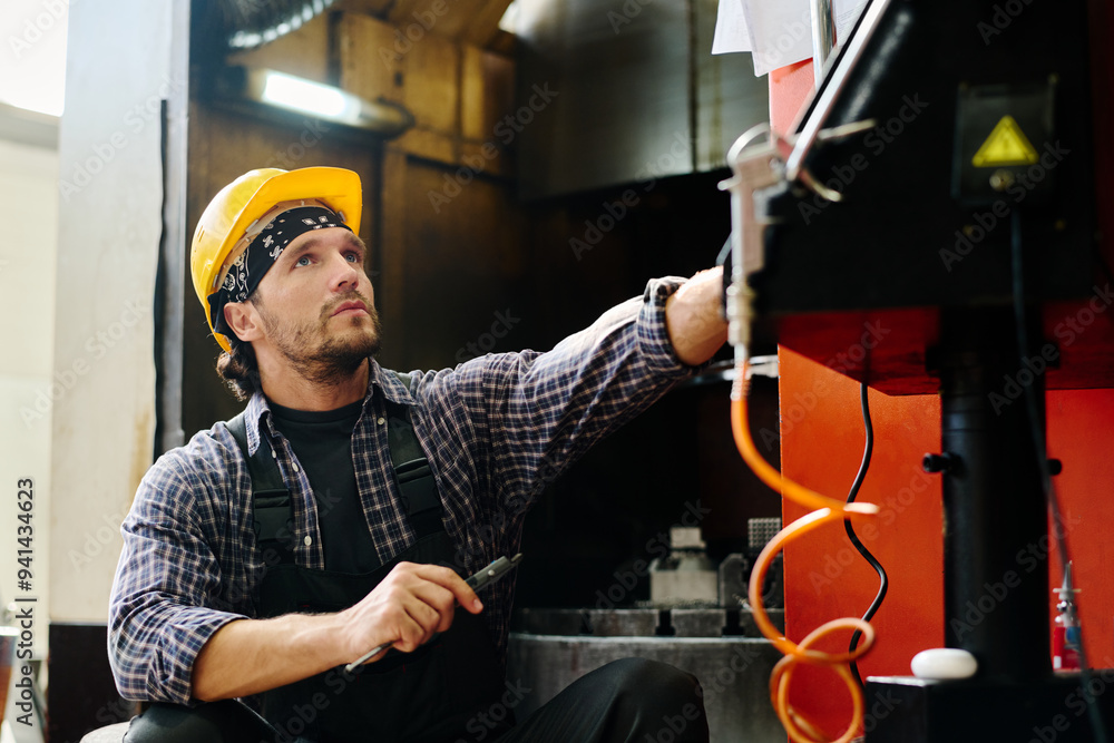 Industrial worker wearing safety gear adjusting machine components ...