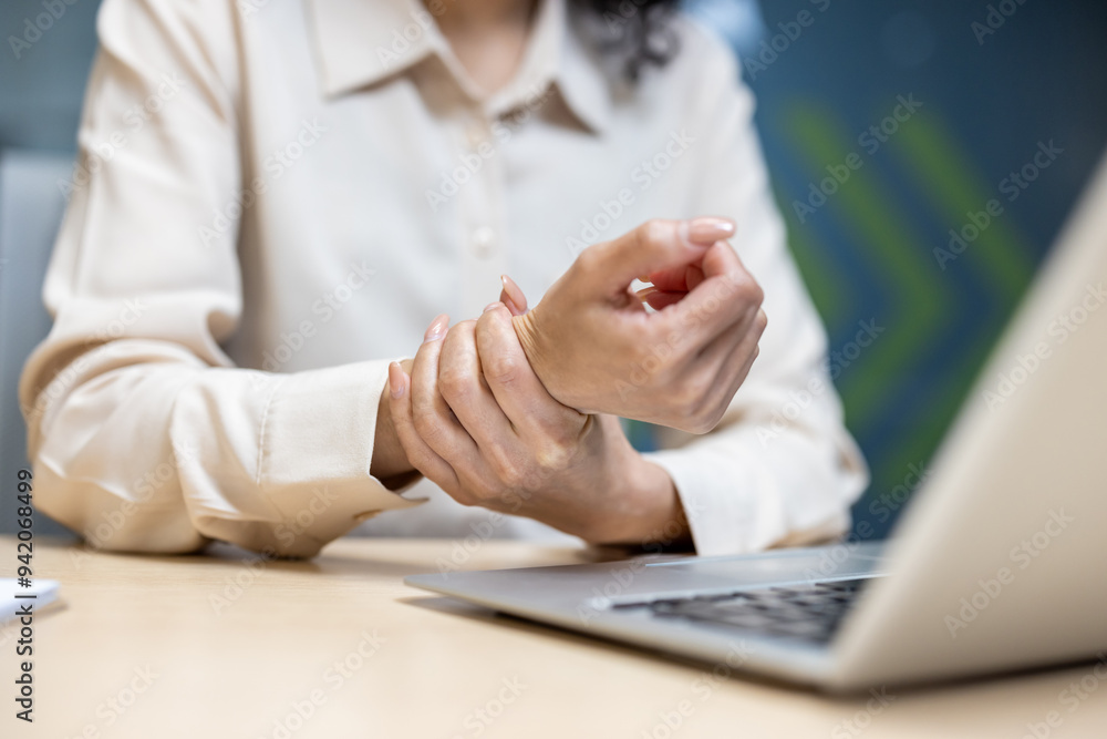 Office worker holds wrist in pain while working on laptop, showing ...