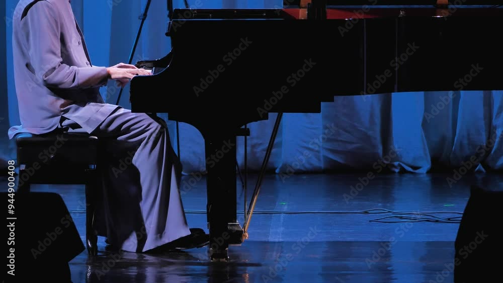 A male pianist playing a grand piano on a stage in a concert hall ...