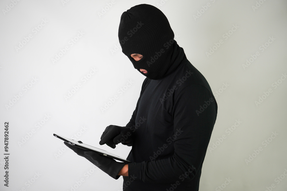 Young Adult black masked robber is holding digital tablet with blank ...