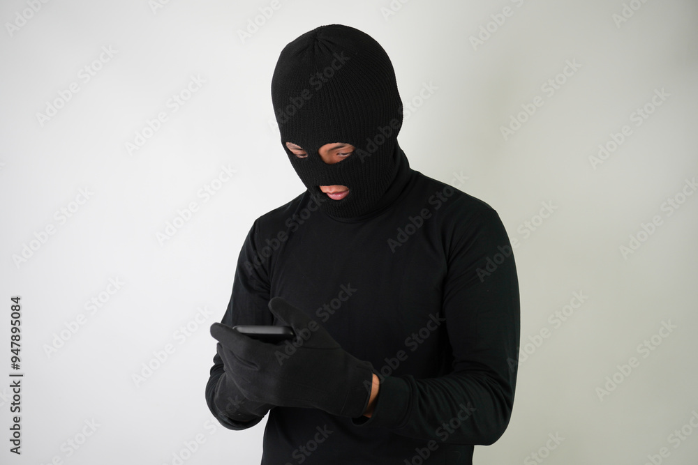 Young Adult black masked robber is holding smartphone with blank green ...