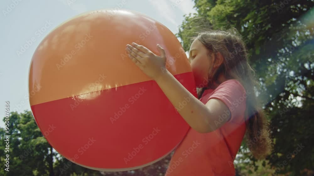 A young girl concentrates as she inflates a large beach ball in the ...