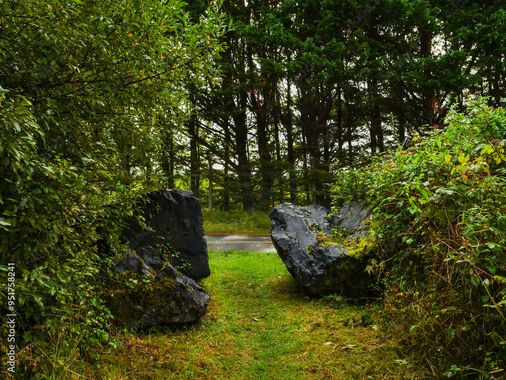 Two huge stone rocks block a way for cars into a forest park foot path ...