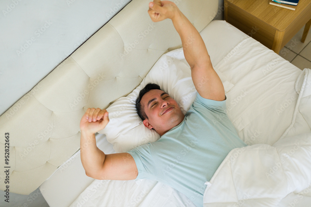 Top view of a man waking up with a smile and stretching in bed, feeling ...