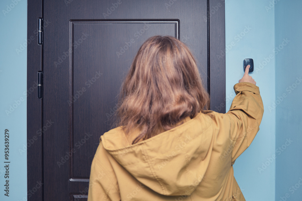 Person in yellow jacket ringing doorbell. Rear view photograph of a ...