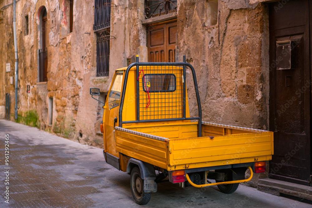 Iconic yellow Piaggio Ape three wheeler on an antique street of Italy ...
