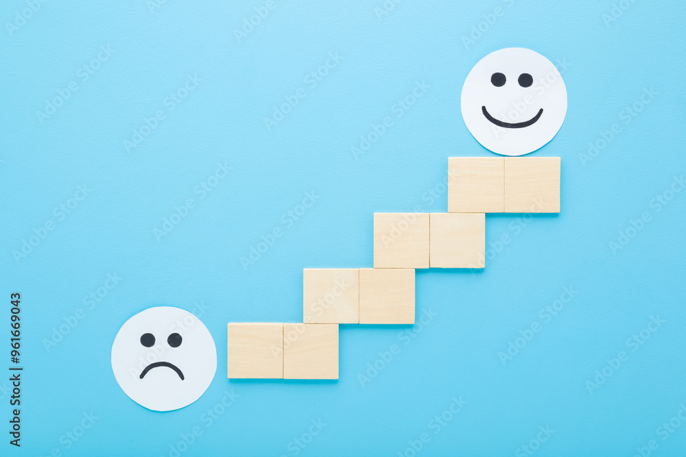Sad and happy smiling faces and wooden bricks ladder on blue table ...