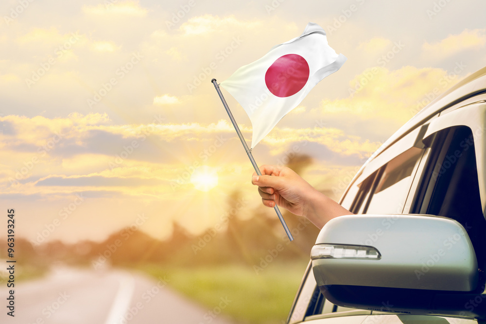 Waving the Japan flag against the sunrise or sunset from a car driving ...