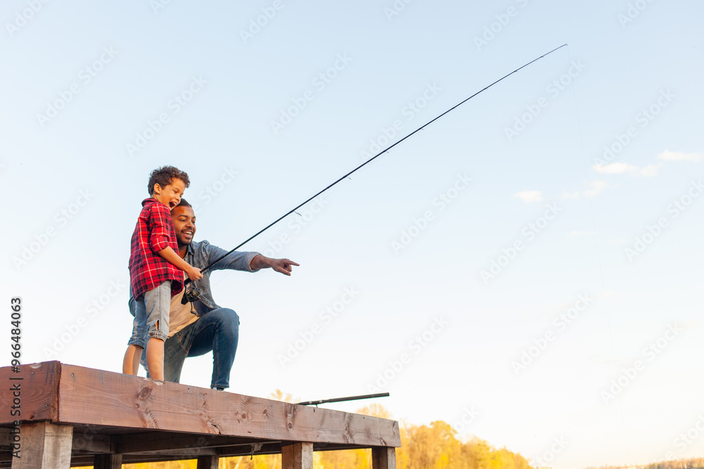 An African American father and his son fish from a wooden pier. The ...