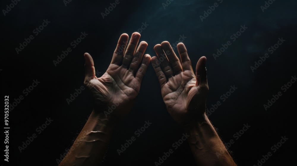 This image shows two hands reaching upward in the dark. The hands are ...