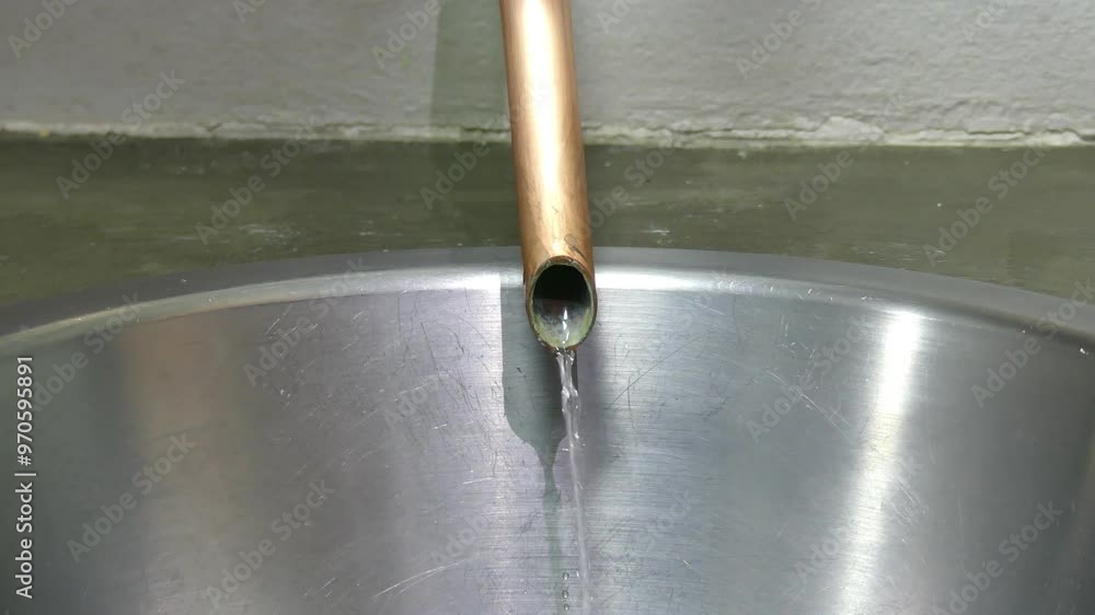 Slow and steady stream of water flowing from a copper pipe into a metal ...