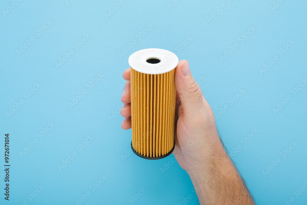 Young man hand holding and showing car new oil filter on light blue ...