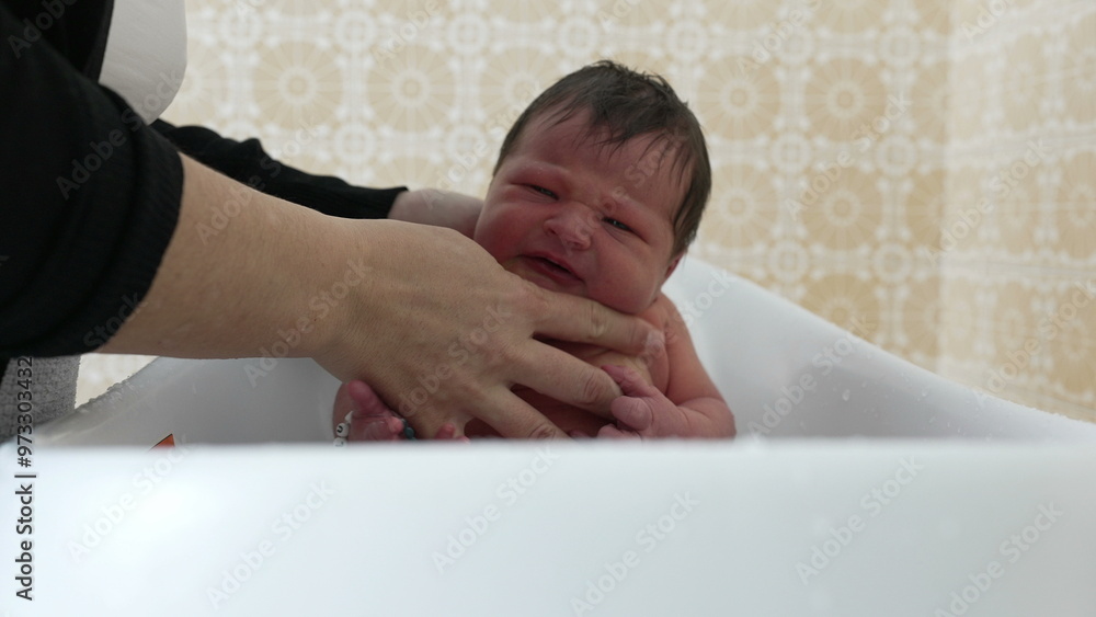 Newborn baby receiving a gentle bath, with water being poured carefully ...