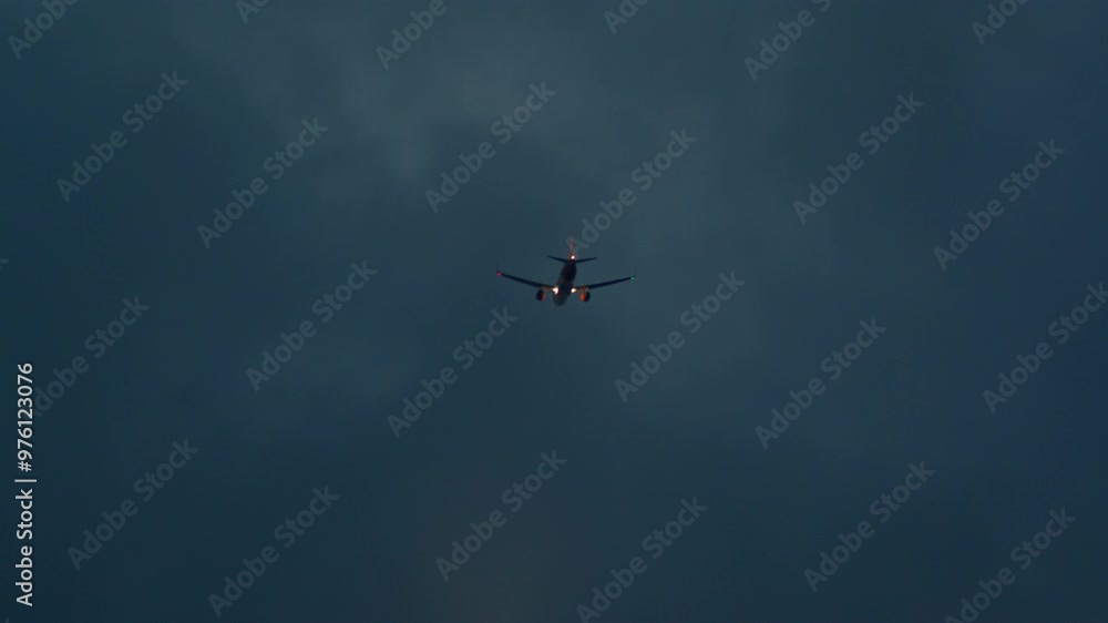 An airplane flying in the dark sky with its lights on, leaving a faint ...