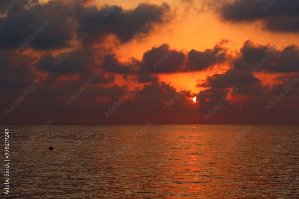 Vivid red orange rising sun, calm morning water surface under the heavy ...