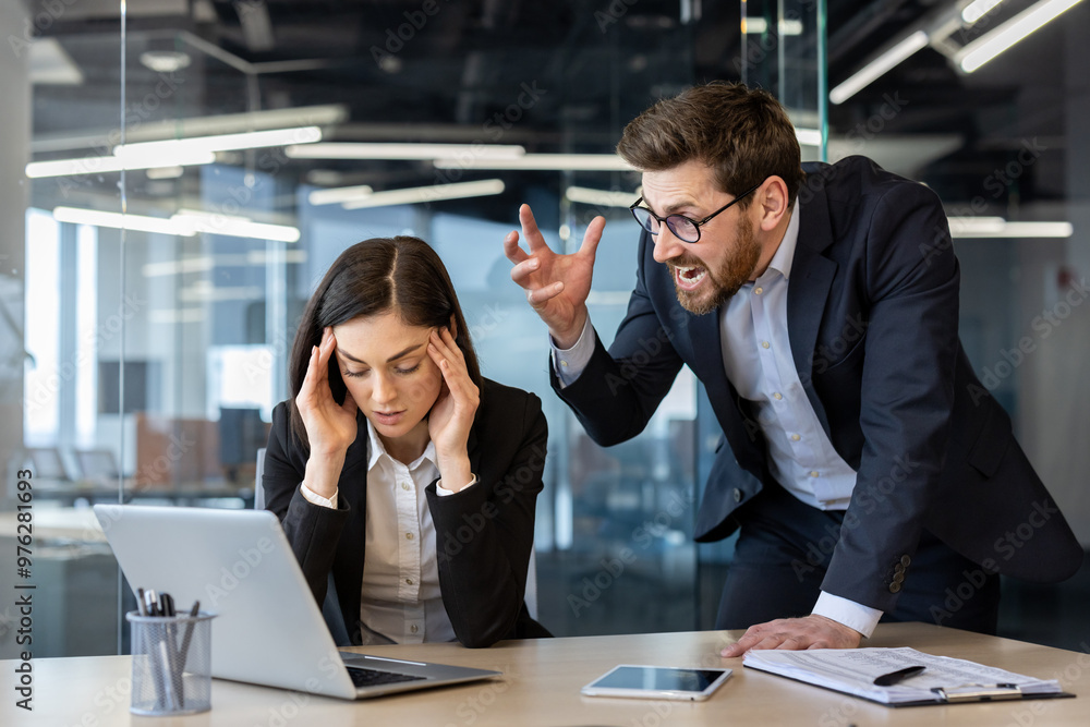 Angry boss yelling at stressed female office worker seated at desk with ...