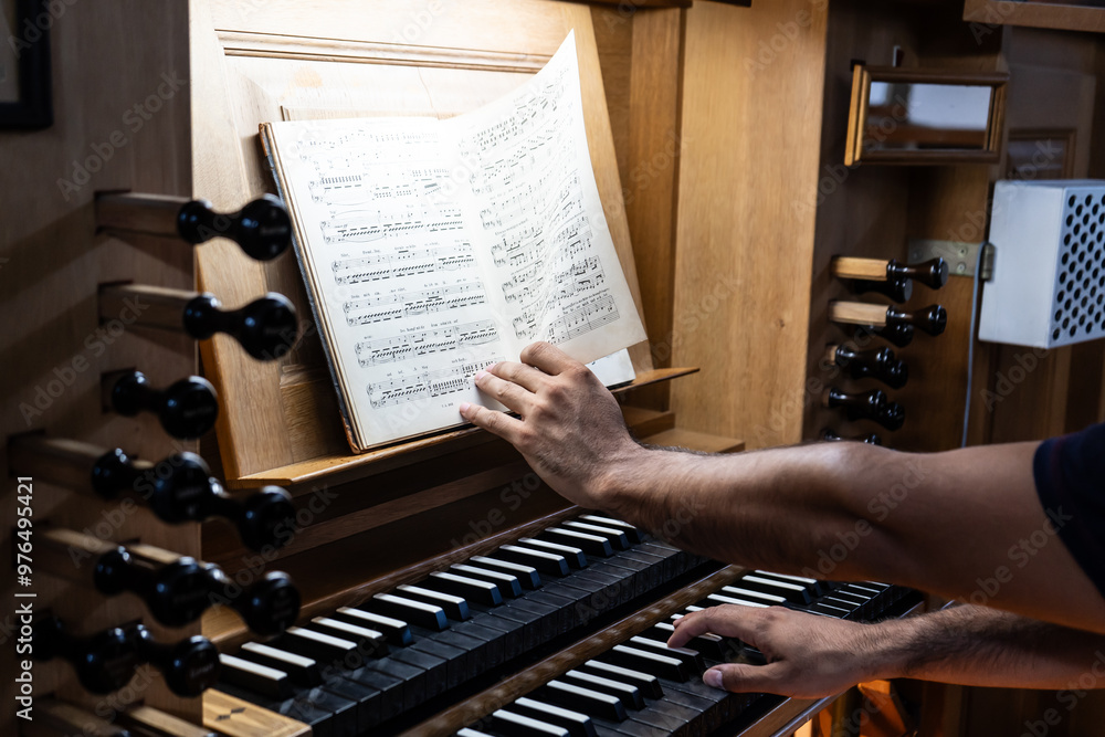 Left side view of Organist playing organ and turning page of musical ...