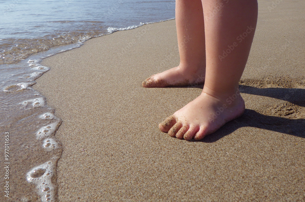 Legs of children stand on the beach. Baby feet in the sand. Closeup ...