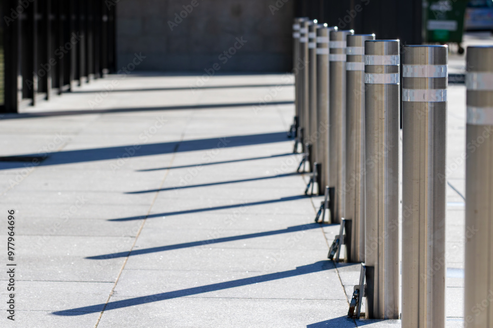 Upright steel parking posts casting linear shadows to left side. Metal ...