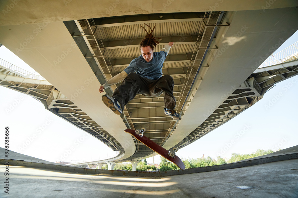 Skateboarder performing trick under large overhead bridge showing skill ...