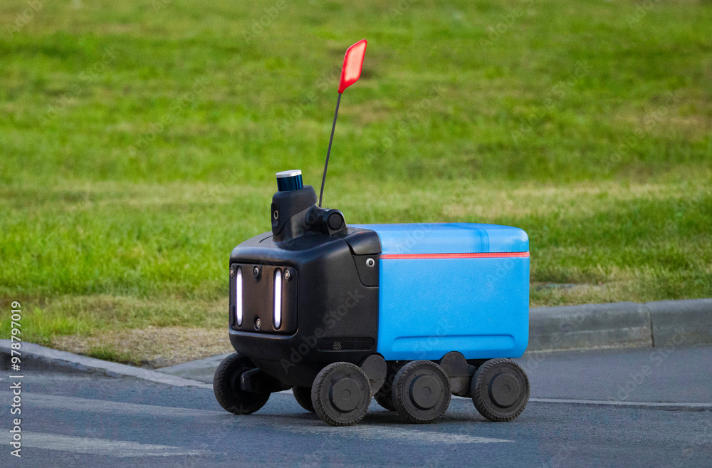 A small blue and black delivery robot with a red flag on top drives on ...
