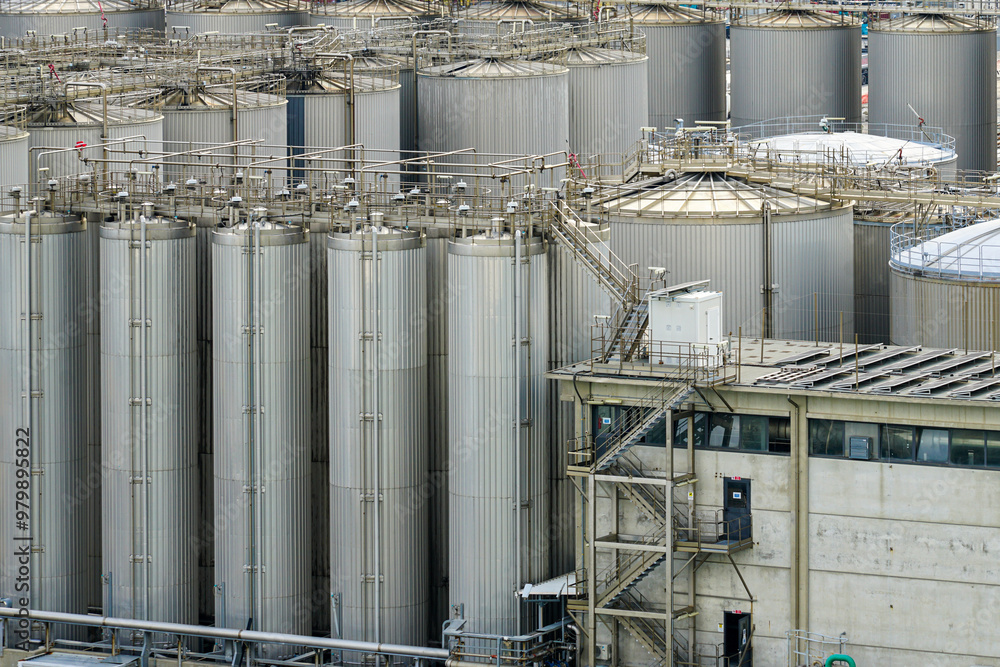 Many tall metal tanks in tank farm, high silos, multiple steel tanks to ...