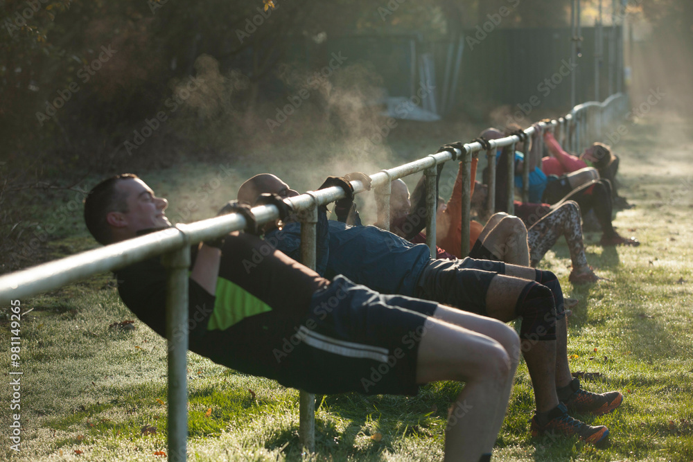Group of people performing outdoor pull-up exercises on a row of bars ...
