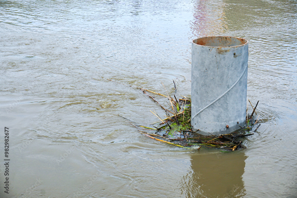 Pipe barrier, partially submerged in water with debris accumulated ...